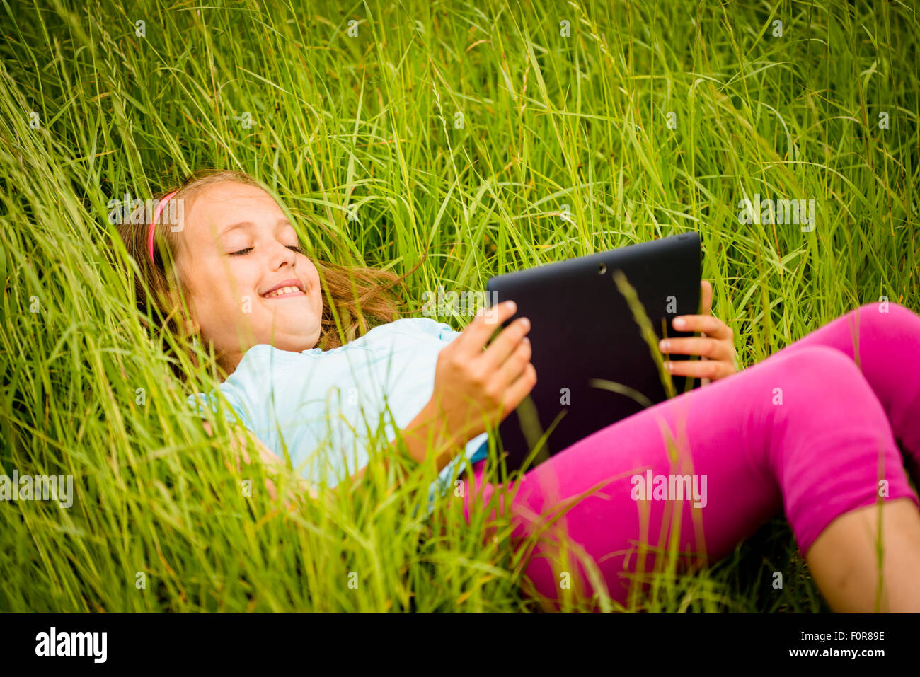Smiling teen girl lying in grass and watching tablet Stock Photo - Alamy