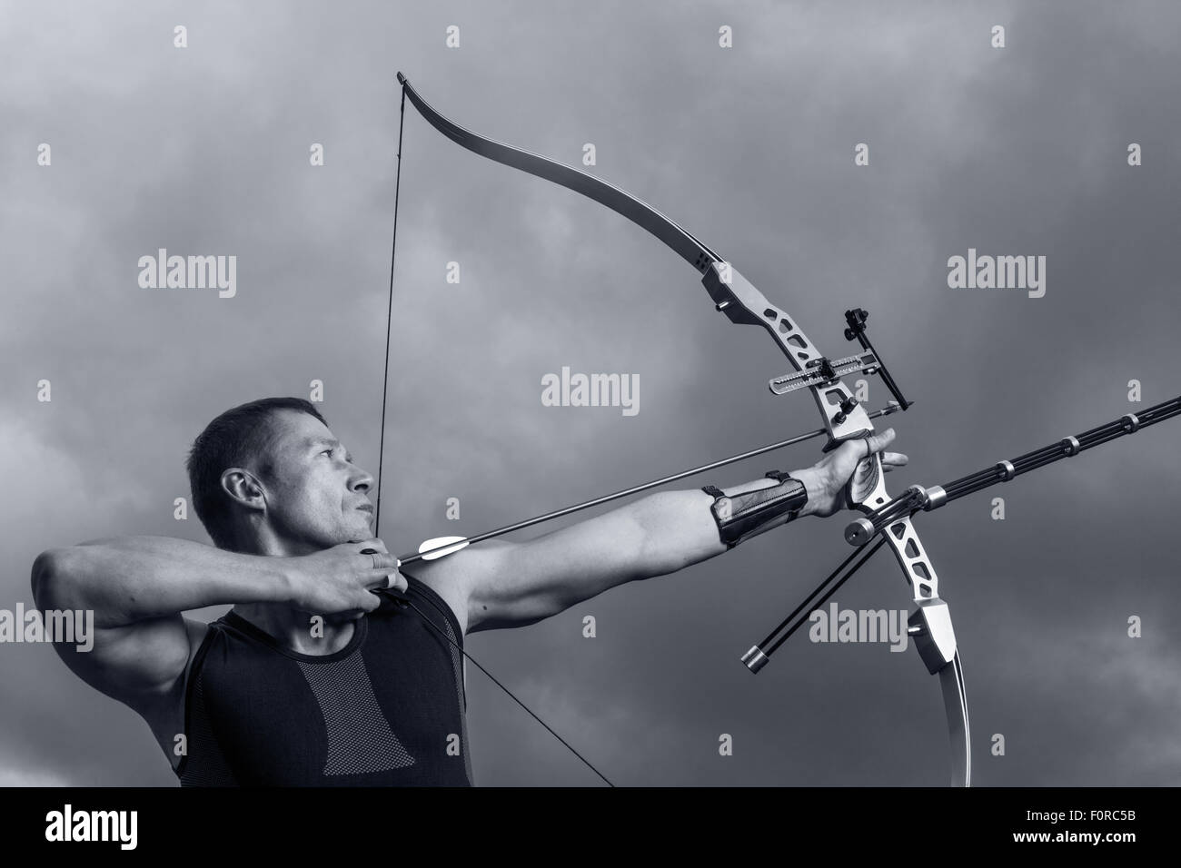 Tough man with bow and arrows, close up with cloudy sky at background ...