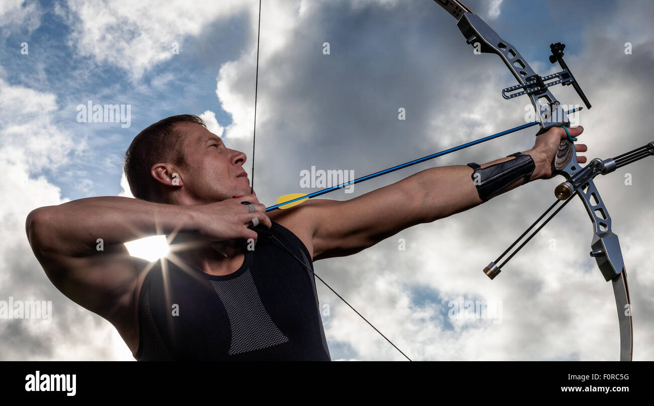 Tough man with bow and arrows, close up with cloudy sky at background ...