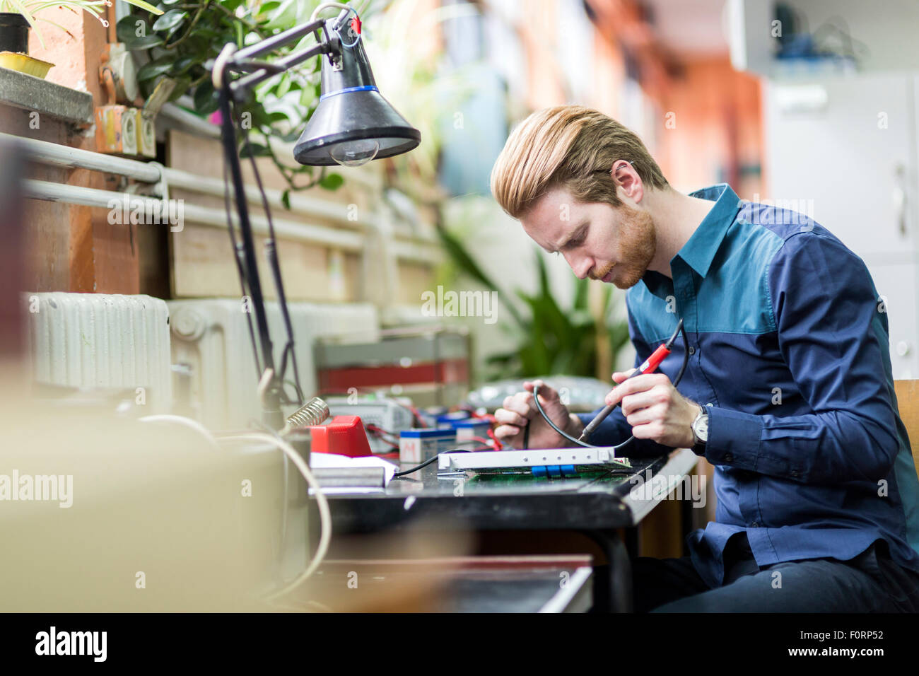 Young handsome man soldering a circuit board and working on fixing ...