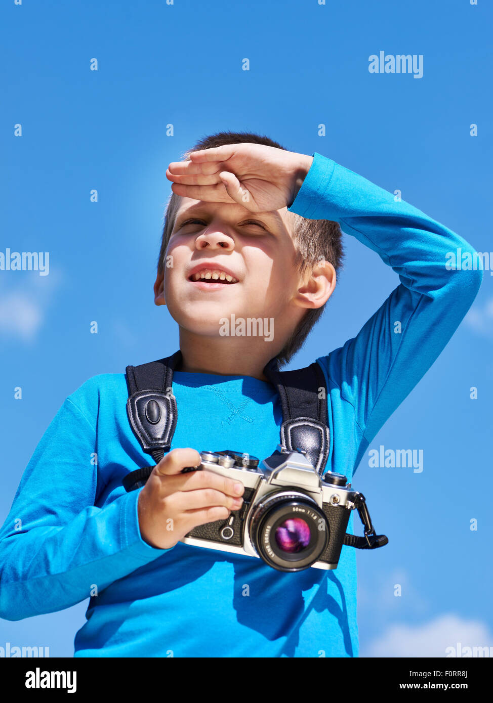 Little boy with retro SLR camera on blue sky looks into the distance ...