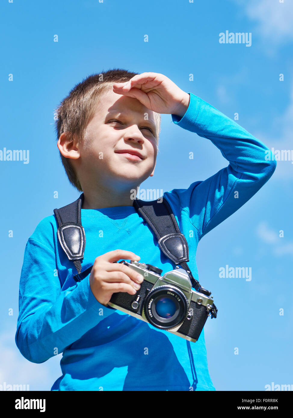 Little boy with retro SLR camera on blue sky looks into the distance ...