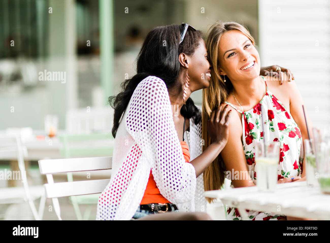 Two attractive women gossiping and whispering outdoors in a cafe in ...