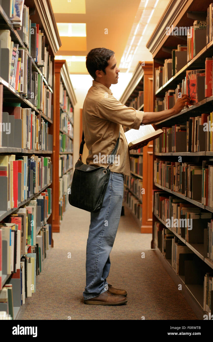 Student looking through books in library aisle Stock Photo - Alamy