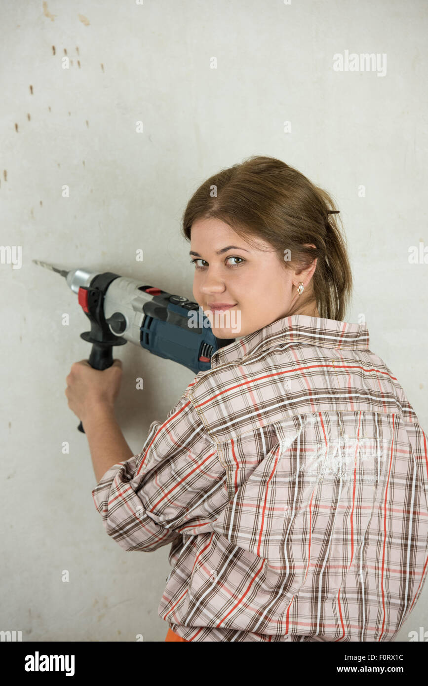 Blond woman holding electric drill and drilling wall Stock Photo - Alamy