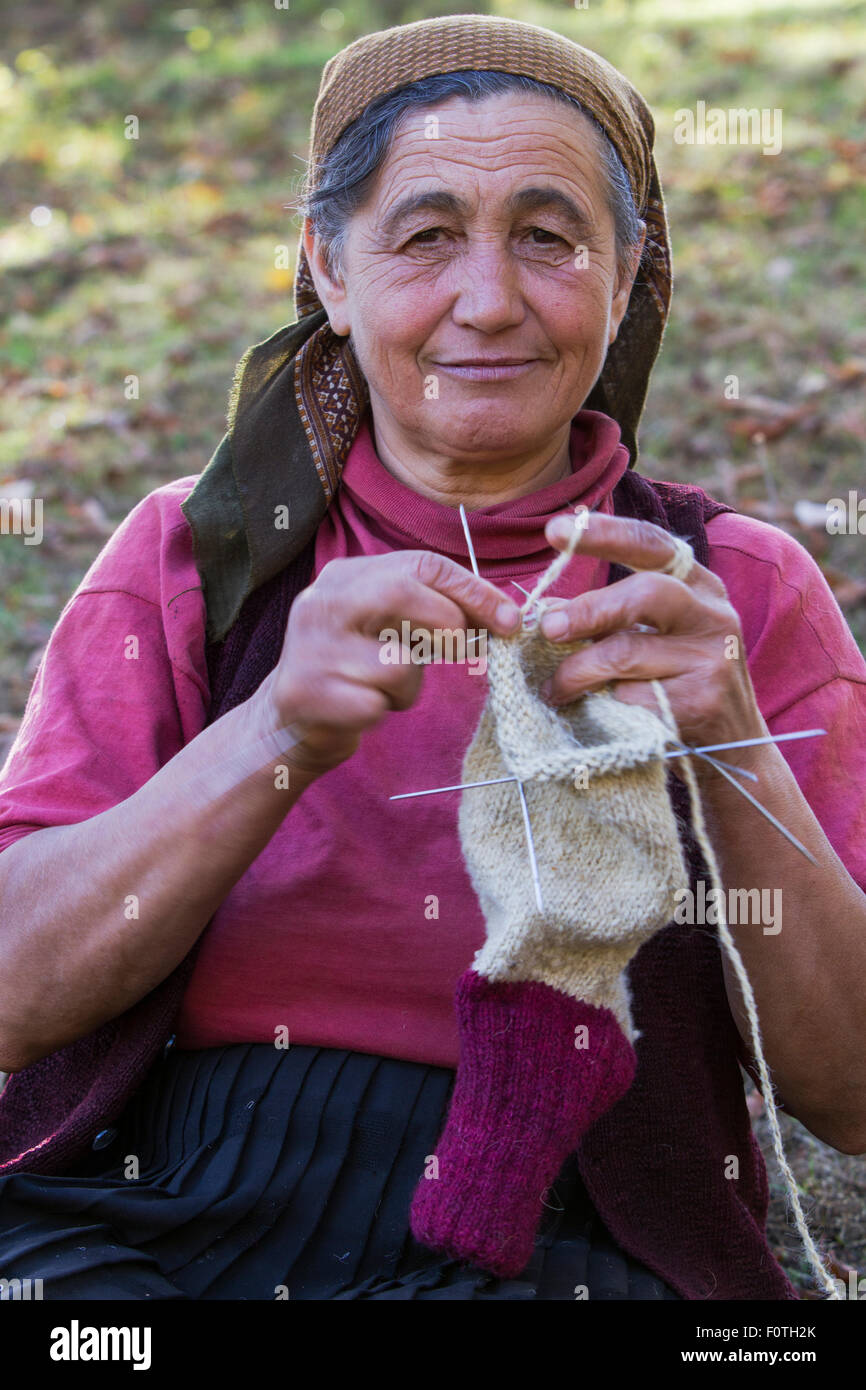Woman (62 years old) knitting socks from own sheep wool in the garden ...