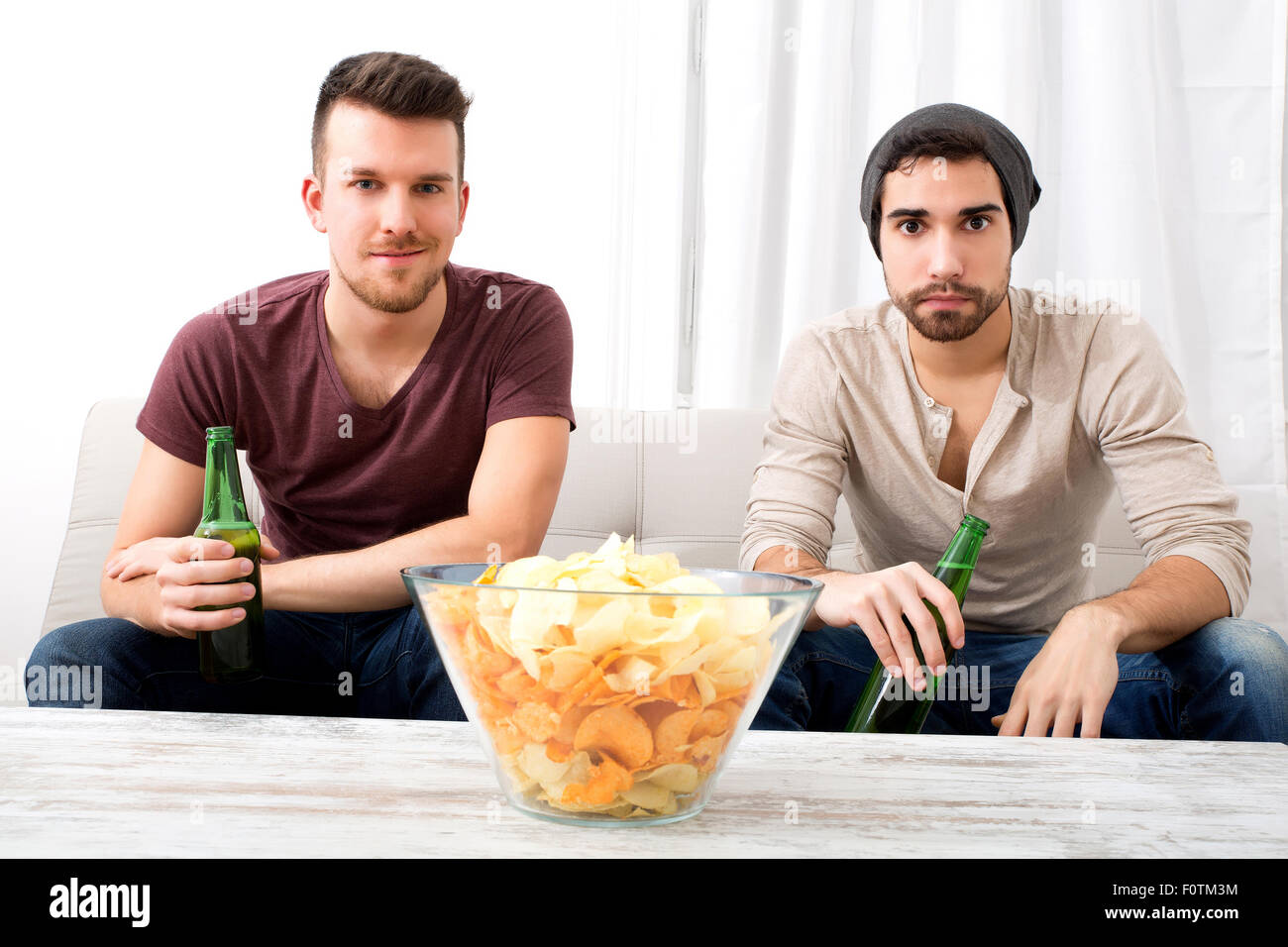 Two guys watching tv, drinking beer, eating crisps at home Stock Photo ...