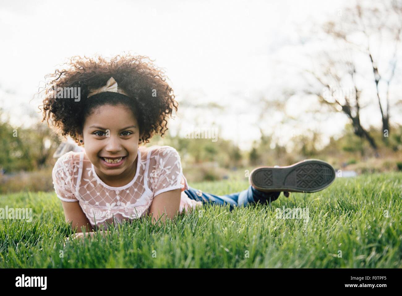 Surface level view of girl lying on front on grass smiling, looking at ...