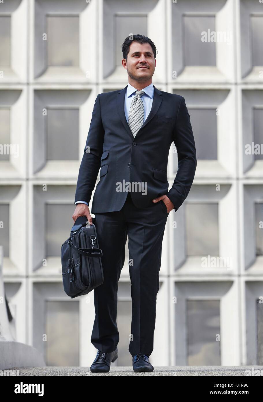 Full length front view of business man, hand in pocket, carrying ...