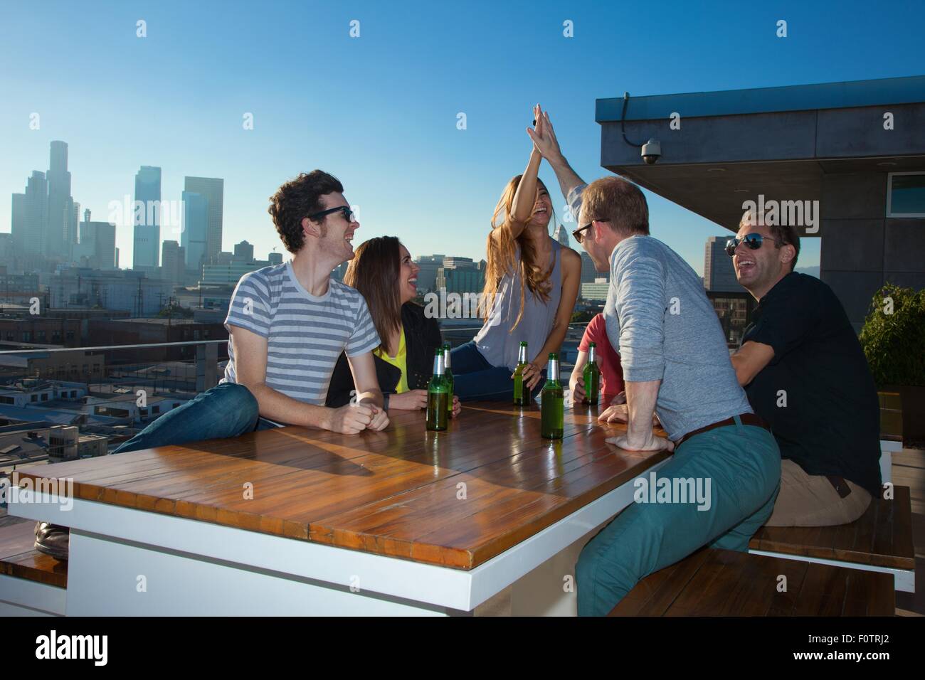 Six adult friends drinking beer at table of rooftop bar with Los ...