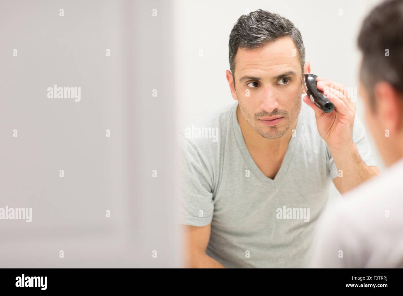 Mid adult man, looking in mirror, using electric shaver Stock Photo - Alamy