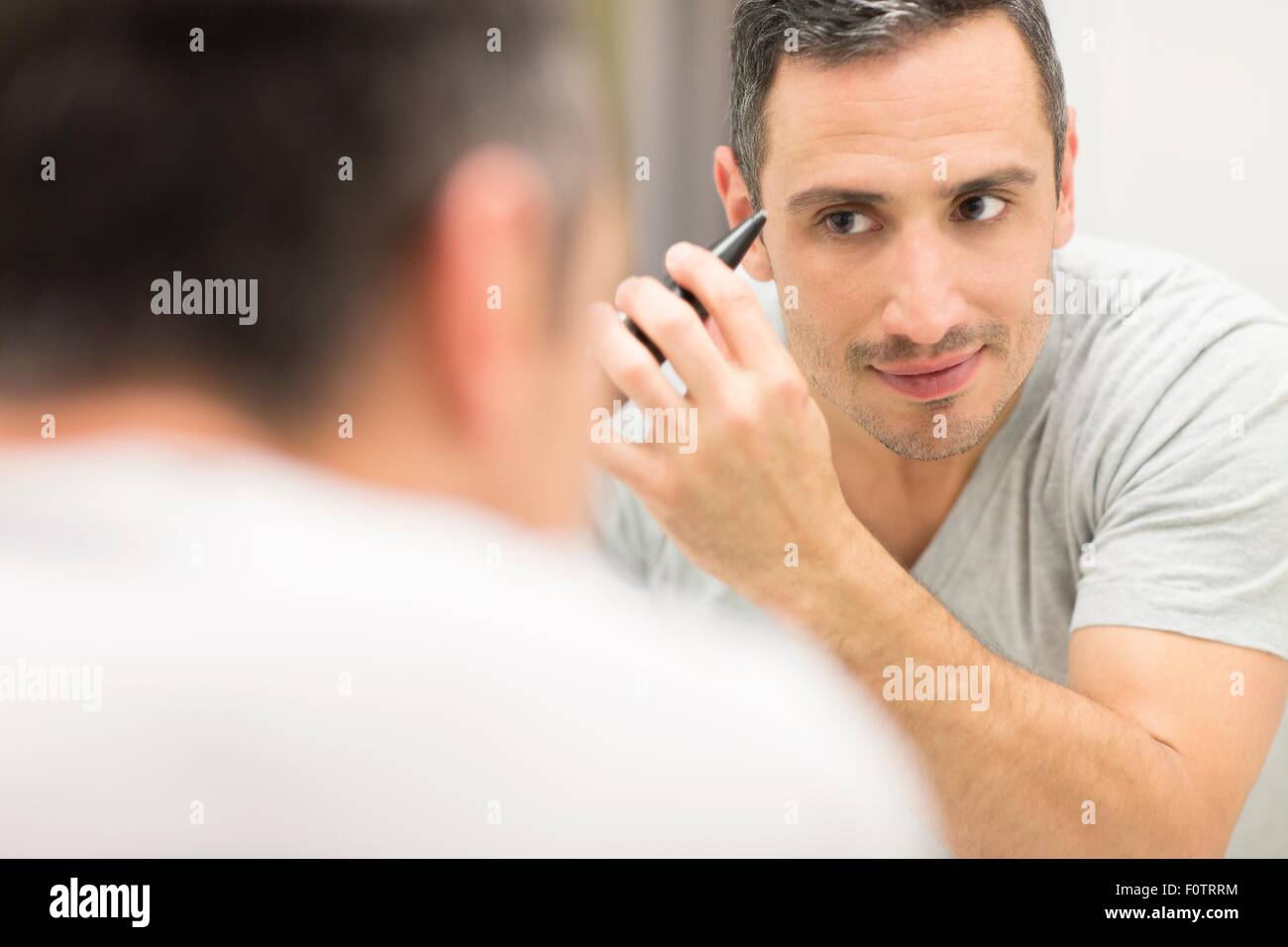 Mid adult man, looking in mirror, using tweezers Stock Photo - Alamy