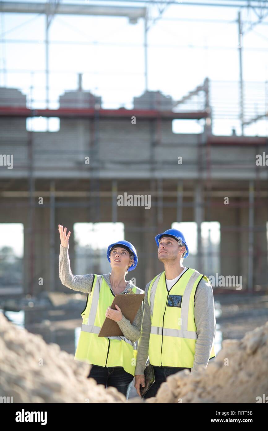 Surveyor looking up whilst talking to builder on construction site ...