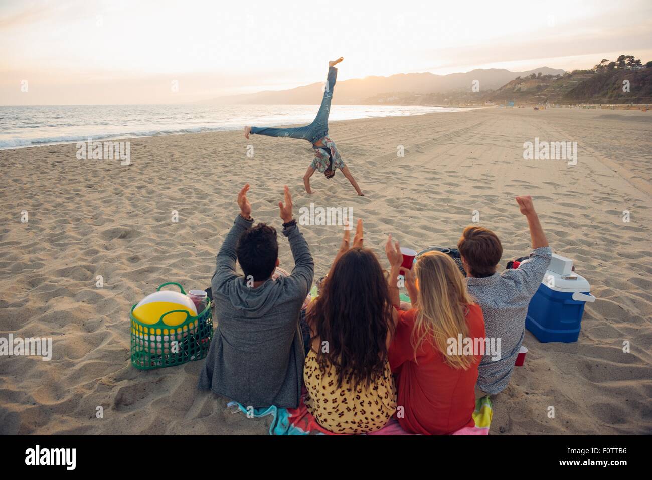 Group of friends sitting on beach, watching friend do cartwheels on and ...