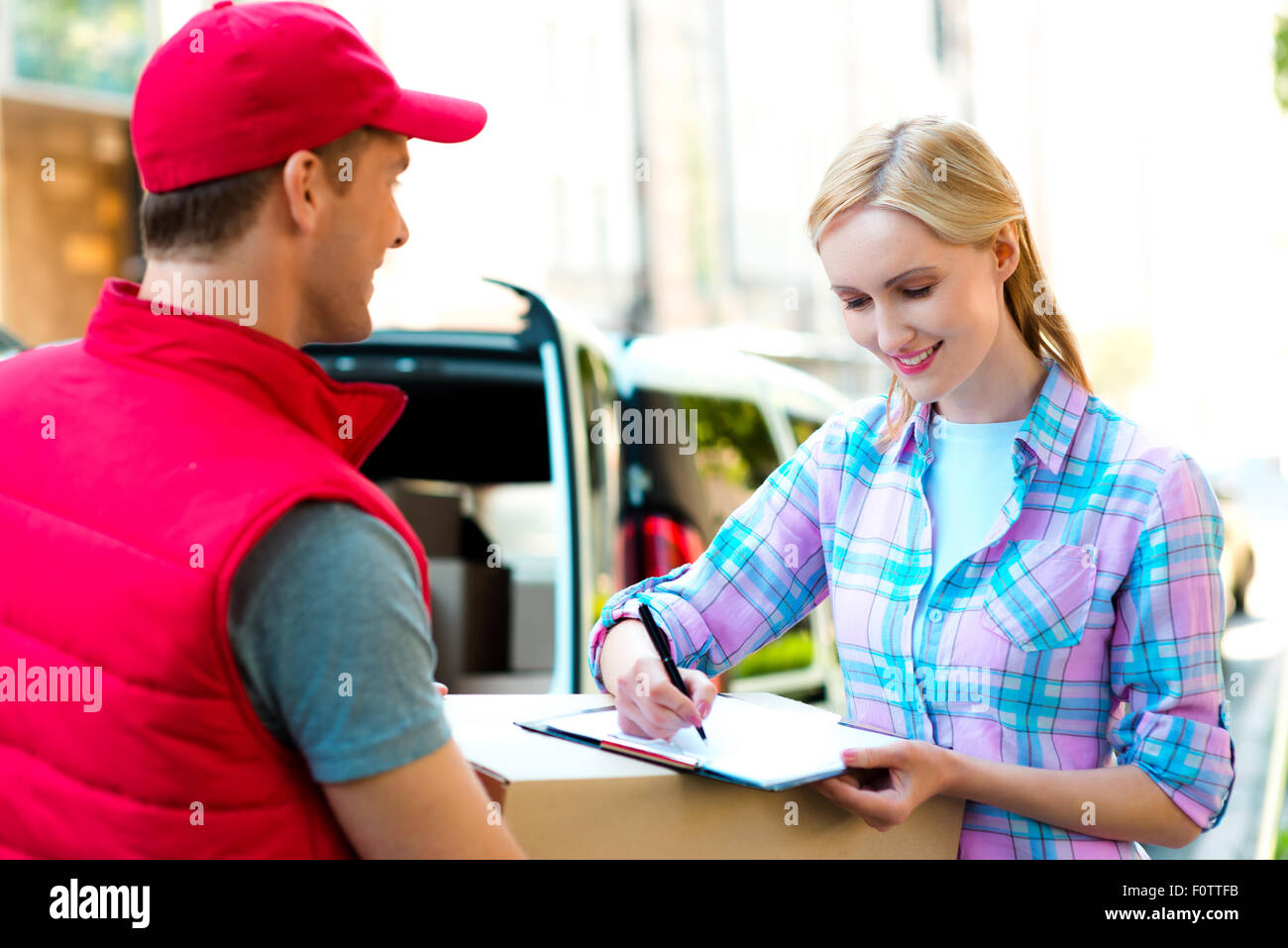 Sign here please! Smiling young delivery man holding a cardboard box ...
