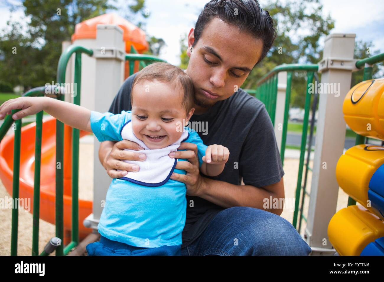 Young man guiding toddler brother on playground slide Stock Photo - Alamy
