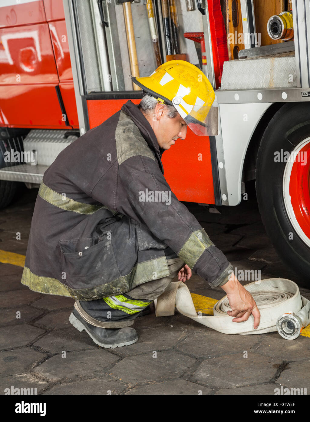 Side view of male firefighter crouching while holding hose by truck at ...