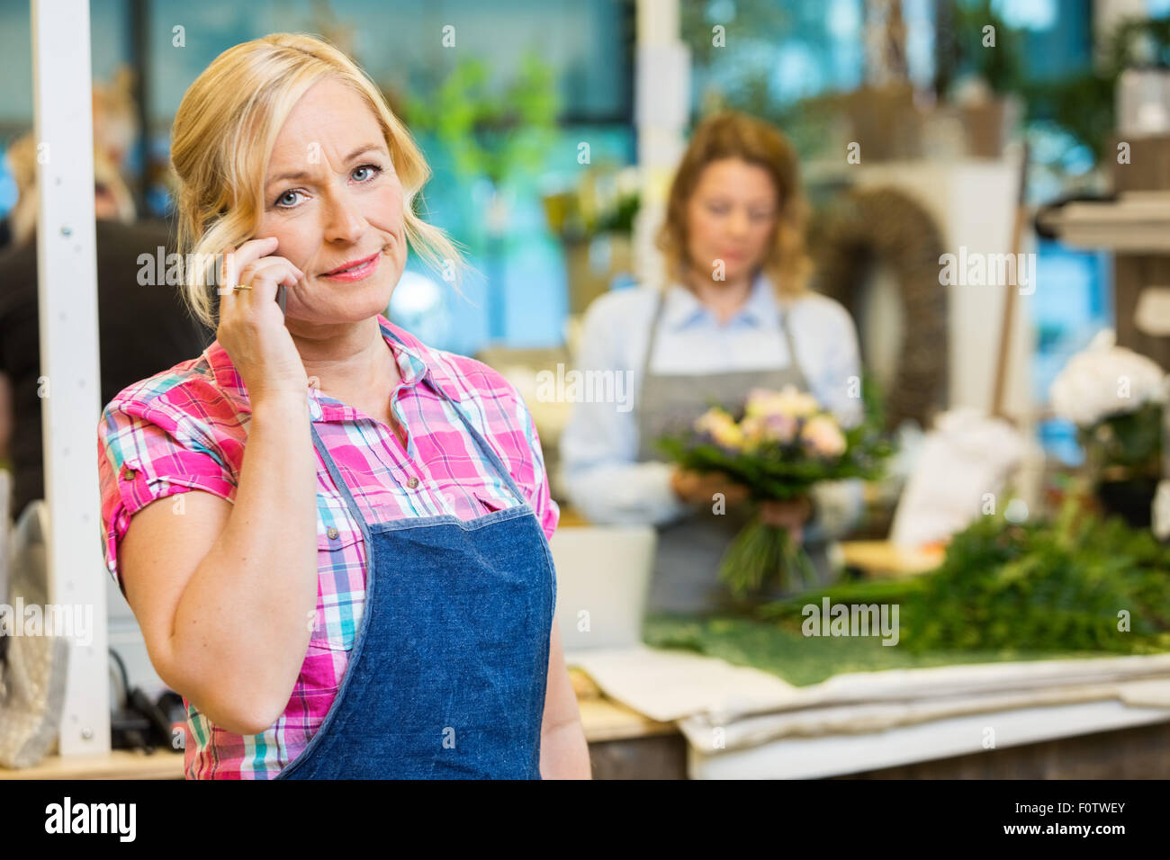 Portrait of mature female florist using mobile phone with colleague ...