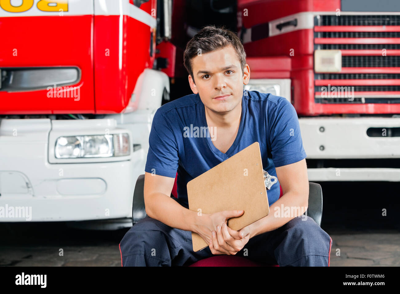 Firefighter Holding Clipboard While Sitting Against Firetrucks Stock ...