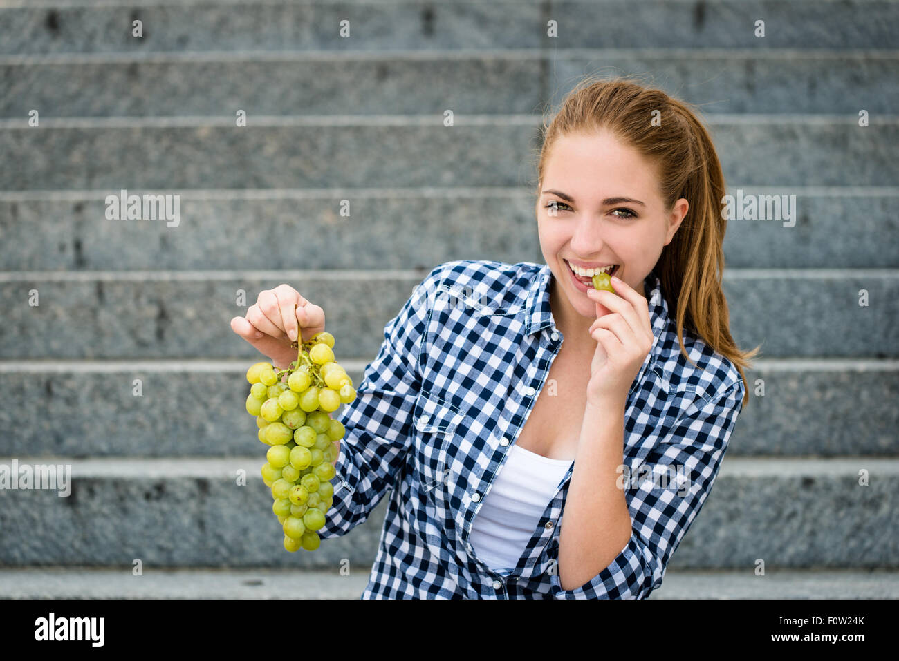 Young woman - teenage girl eating grapes outdoor sitting on stairs ...