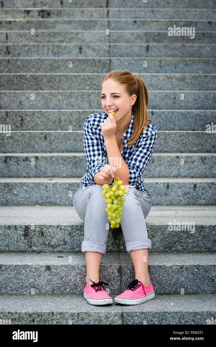 Young woman - teenage girl eating grapes outdoor sitting on stairs ...