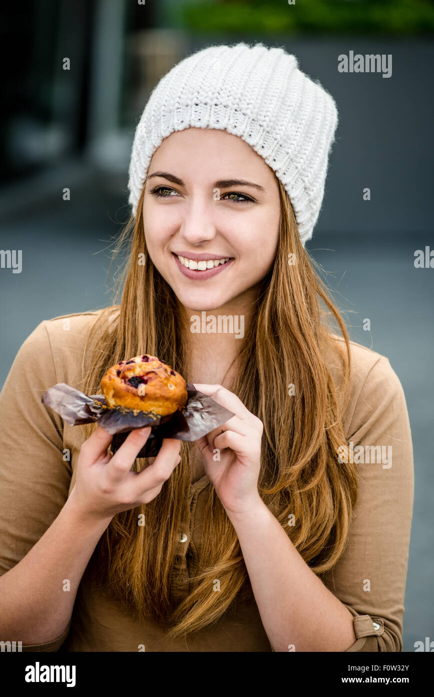 Young woman - teenager in cap eating muffin outdoor in street Stock ...