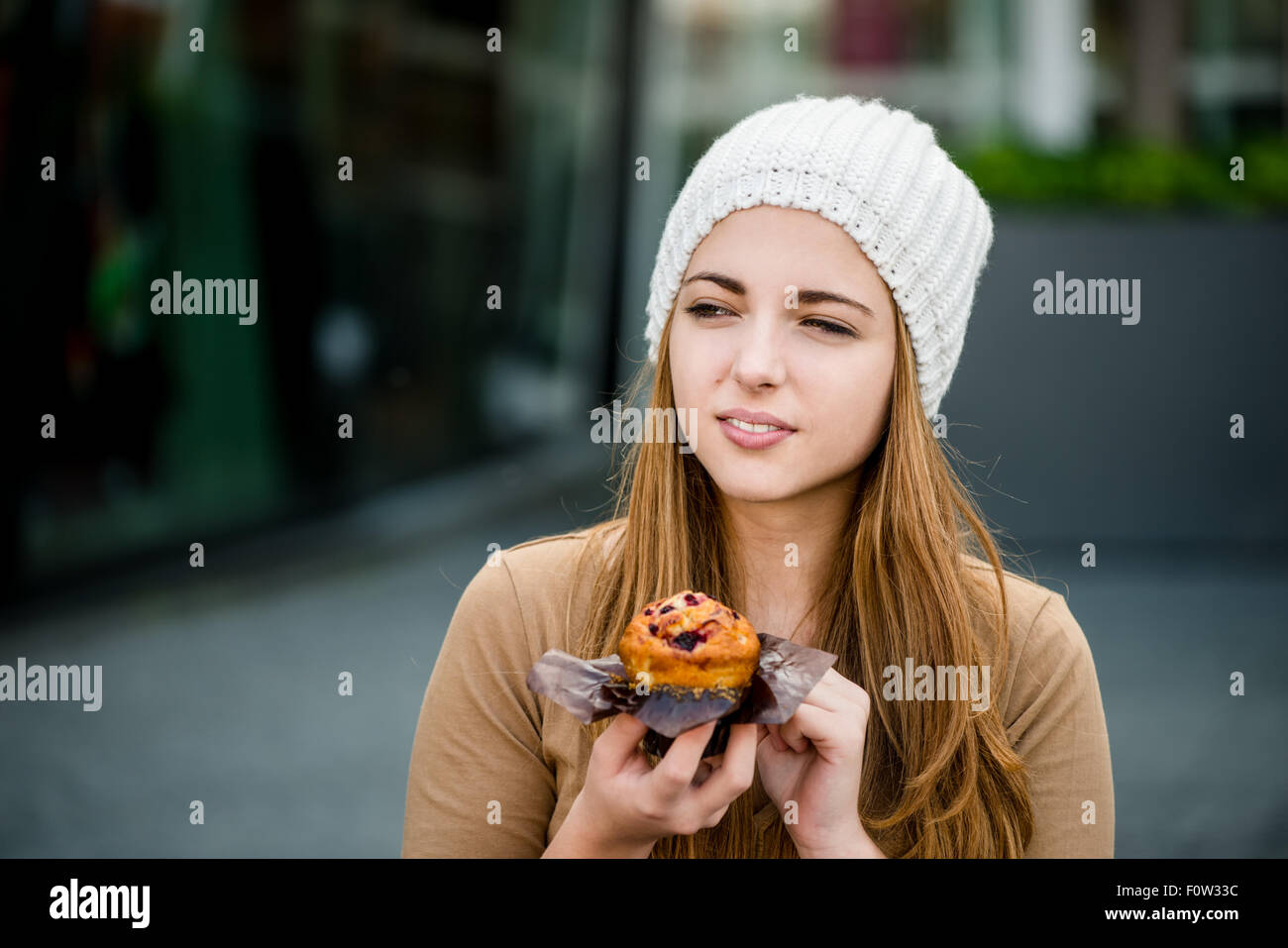 Young woman - teenager in cap eating muffin outdoor in street Stock ...