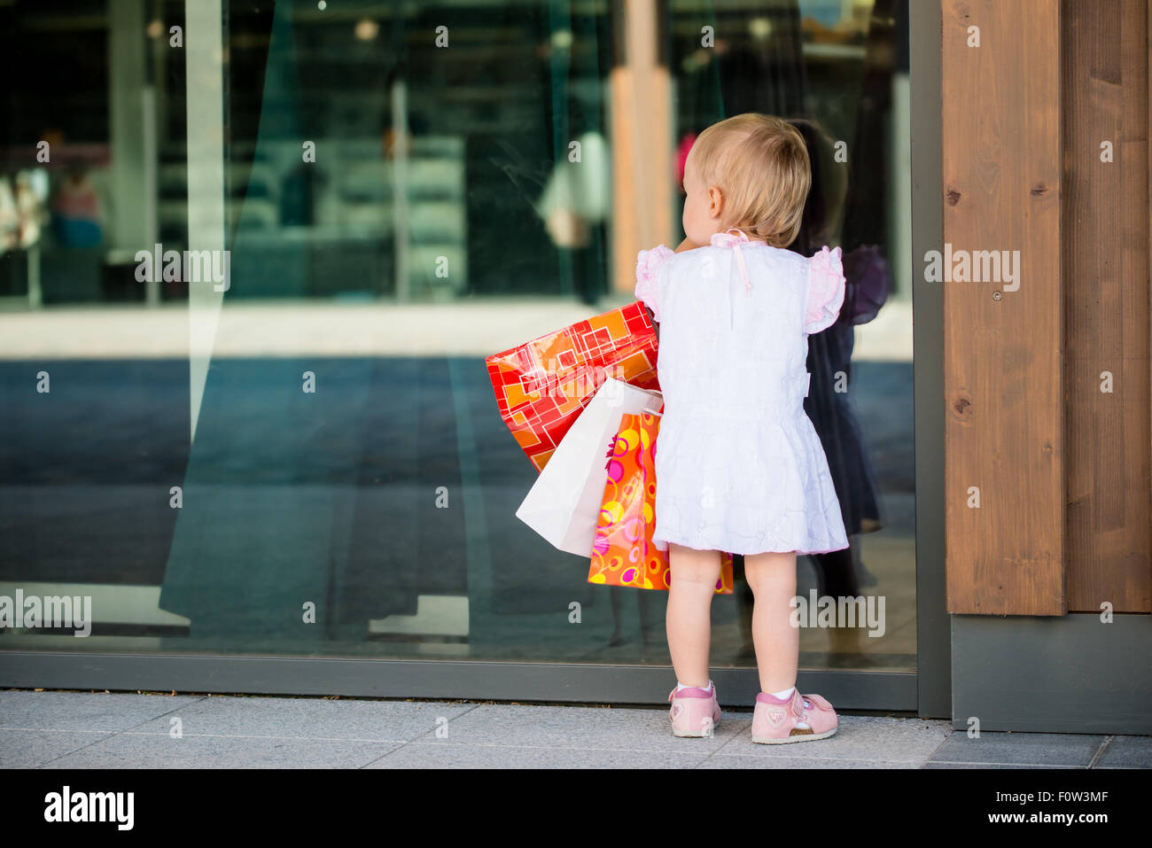 Little girl in white dress looking through shop window Stock Photo - Alamy