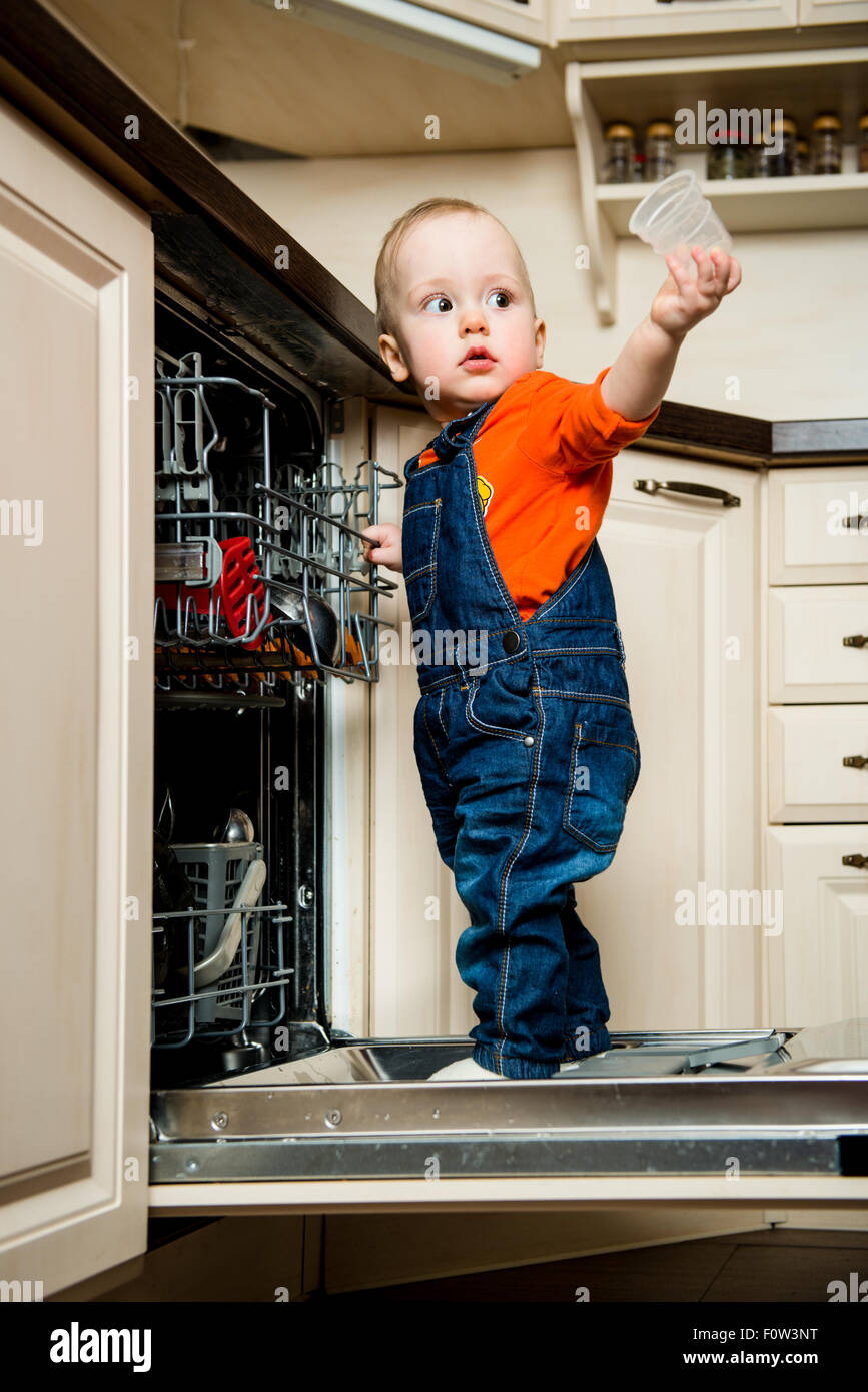 Cute baby standing on dishwasher in kitchen and helps it unload Stock ...