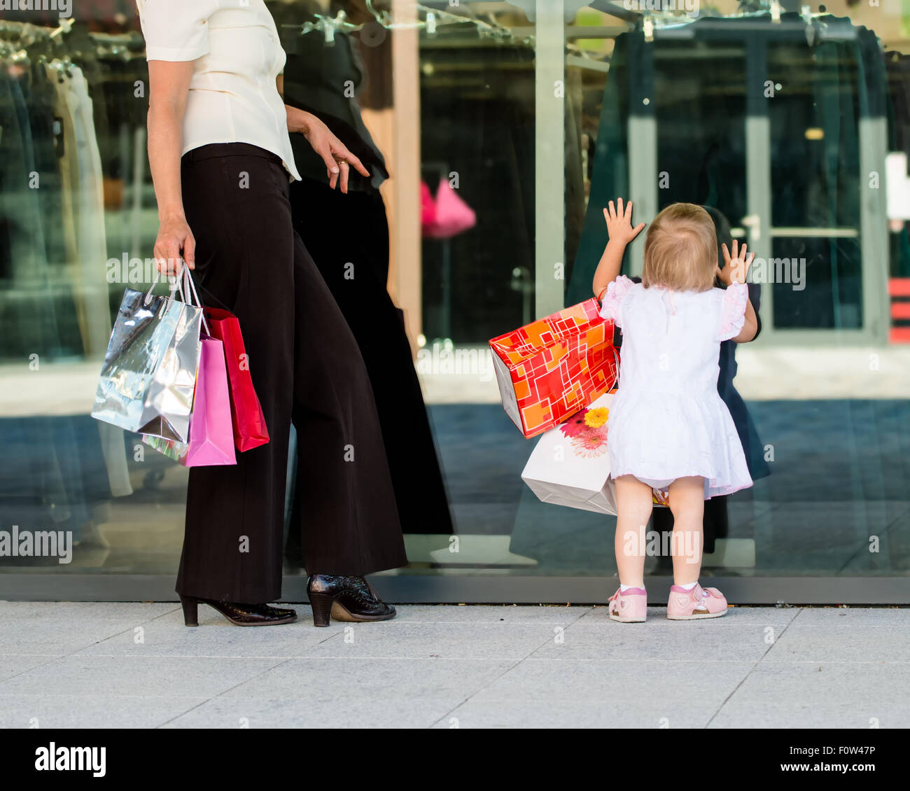 Mother with little girl in white dress looking through shop window ...
