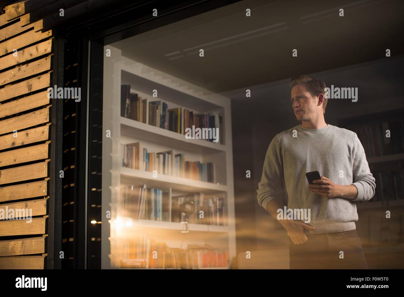 Man with smartphone looking out of window at home, Tokavaig, Isle of ...