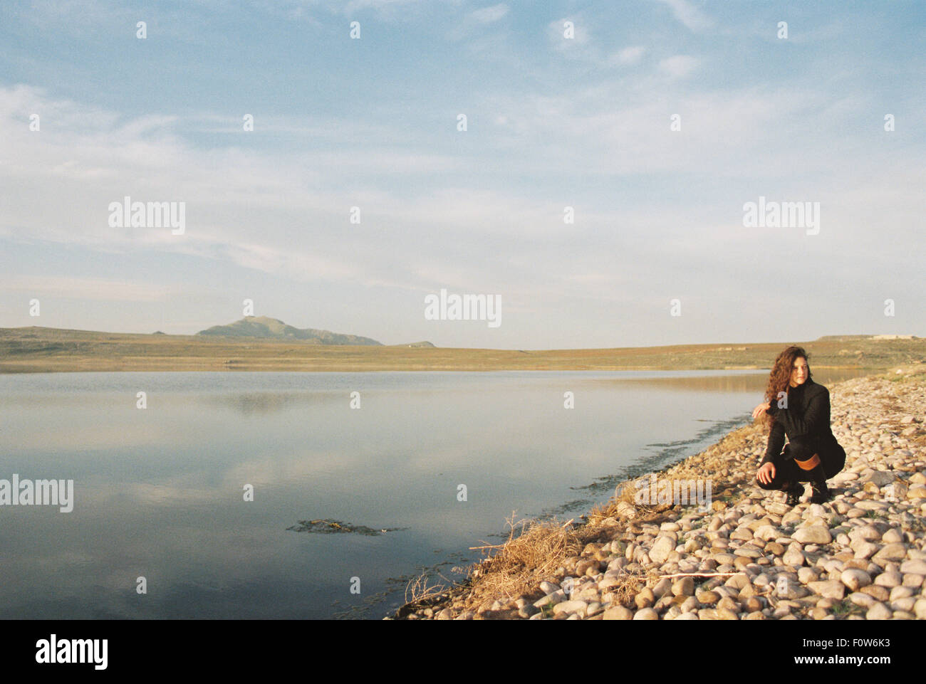 A woman collecting pebbles on the shore of a lake Stock Photo - Alamy