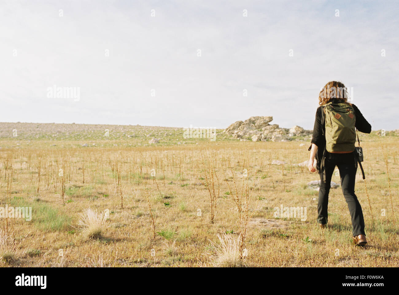A woman walking across open ground wearing a hat, carrying a backpack ...