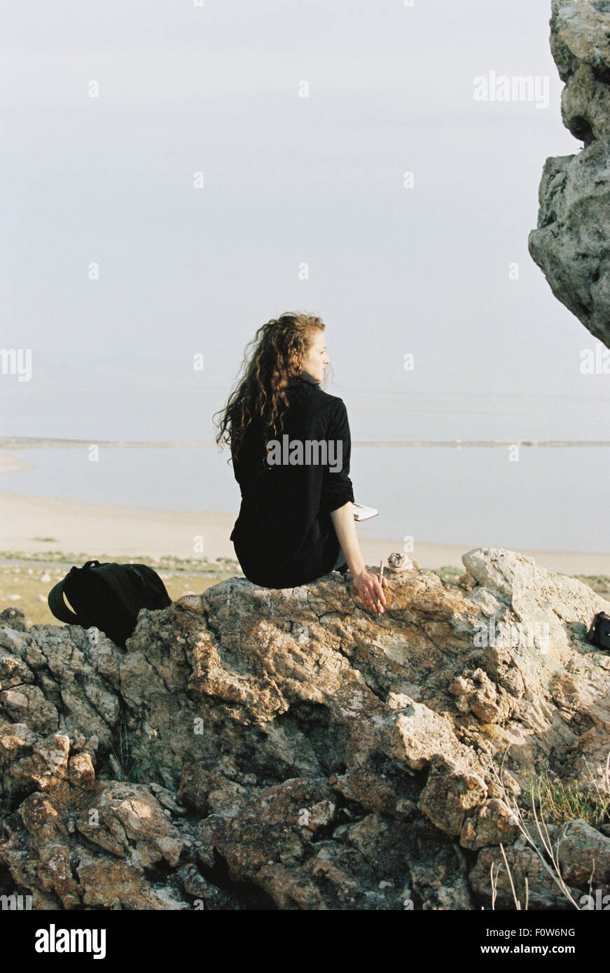 A woman sitting on a rock looking out over water Stock Photo - Alamy