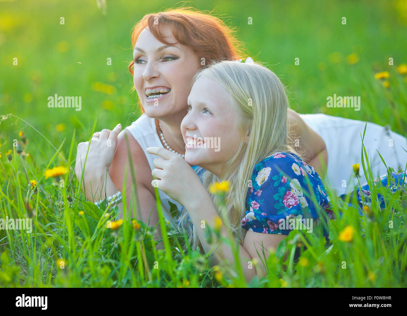 Mom with braces and her little daughter lie on grass smiling at the ...
