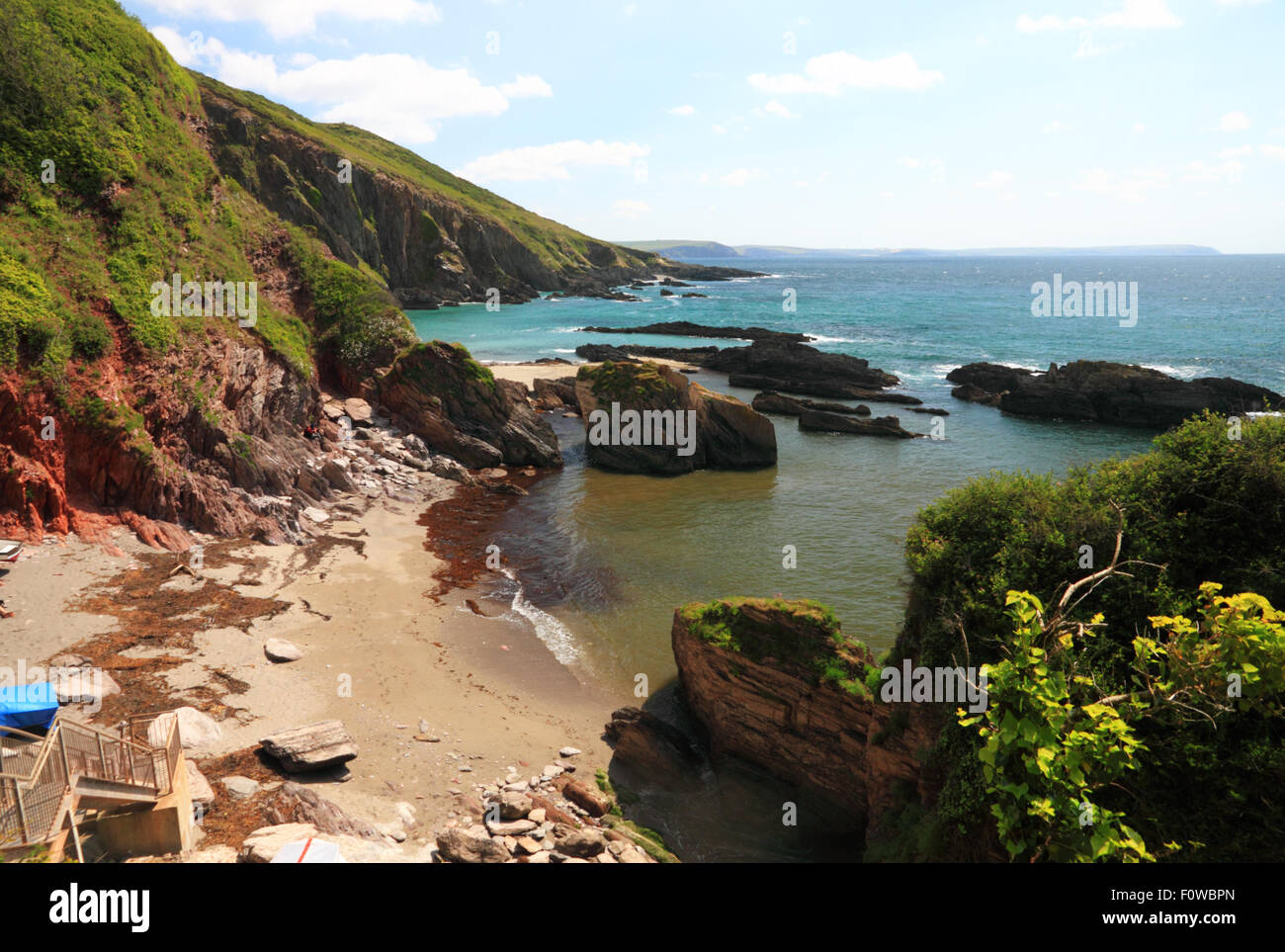 A rocky beach with green cliffs and reddish rocks Stock Photo - Alamy