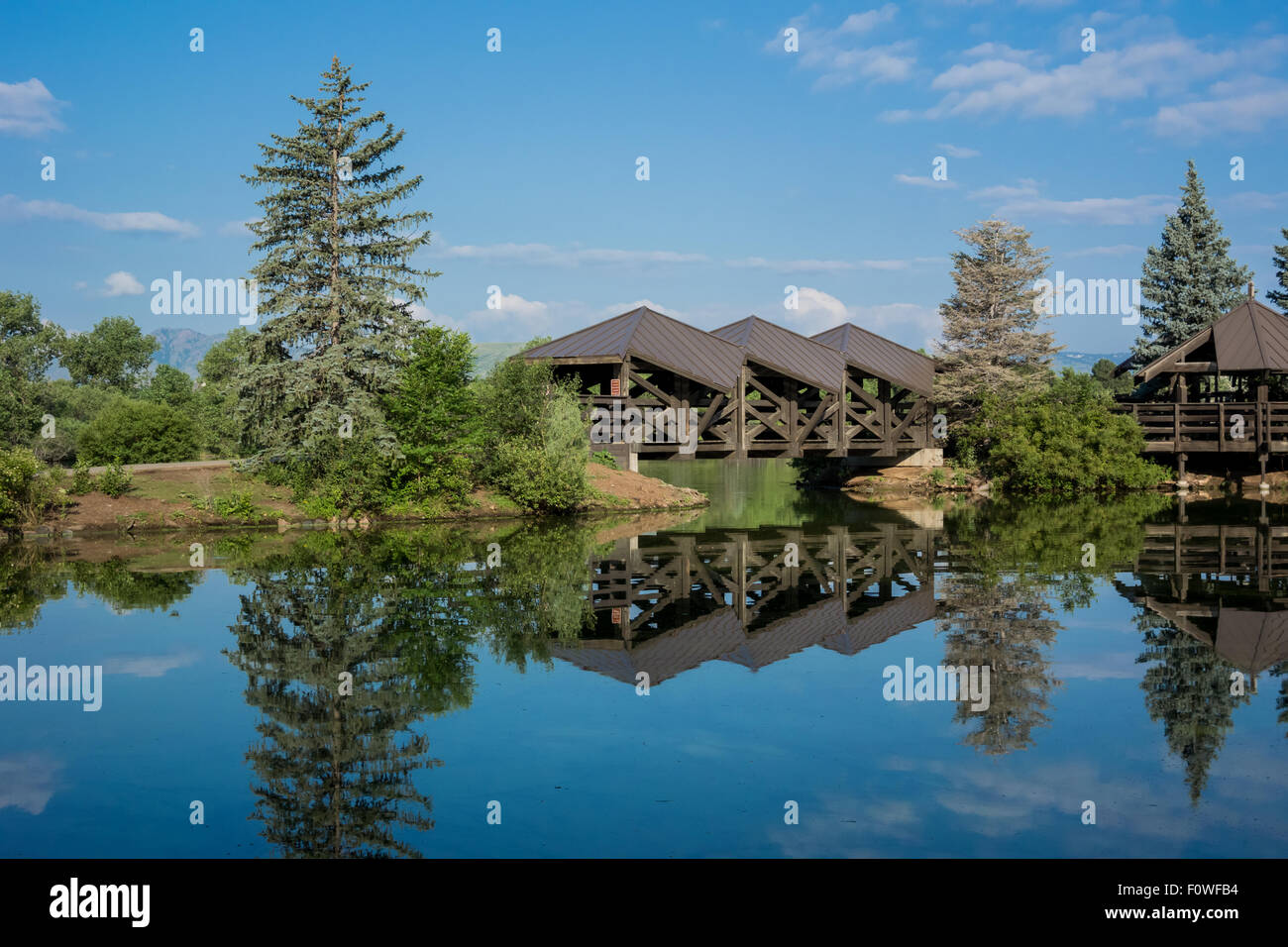 A covered bridge over a calm pond in a public park in Denver, Colorado ...