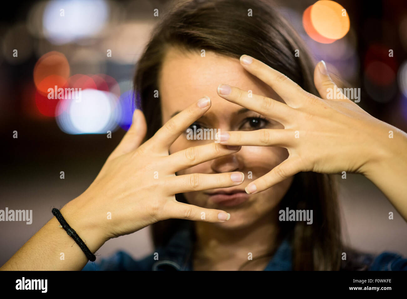 Portrait of young woman outdoor in night street with hands through face ...