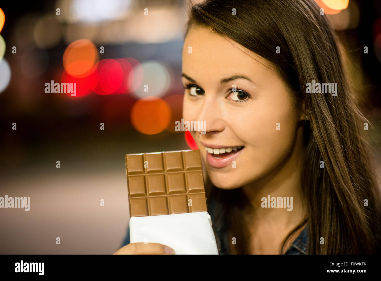 Young woman eating chocolate in street with neon lights at night Stock ...