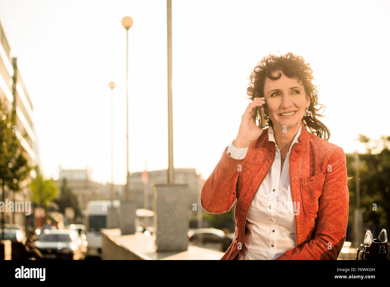 Senior woman in red jacket calling mobile phone while sitting in street ...