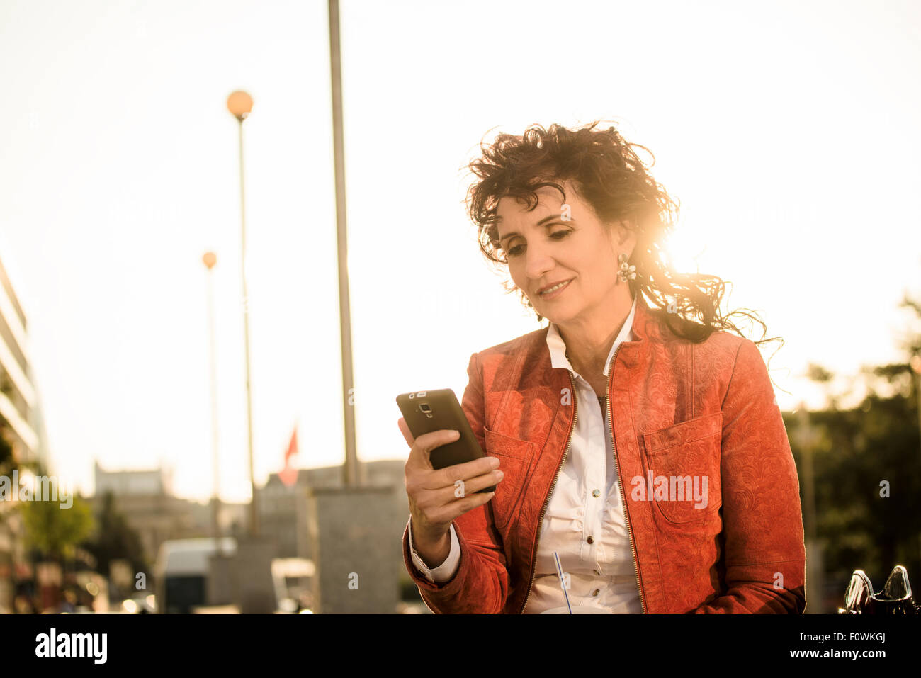 Senior woman in red jacket looking to her mobile phone while sitting in ...