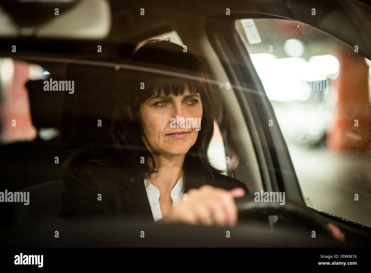 Senior business woman driving car at night - view through front window ...