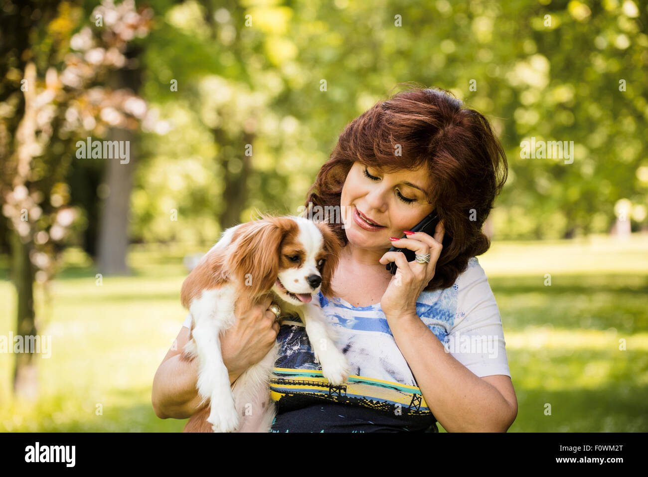 Mature woman calling phone while holding her dog by outdoor in nature ...