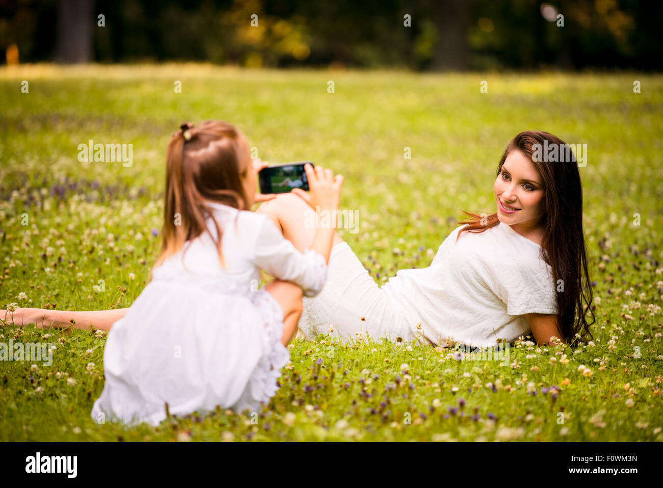 Child taking photo of her mother with phone camera outdoor in park ...