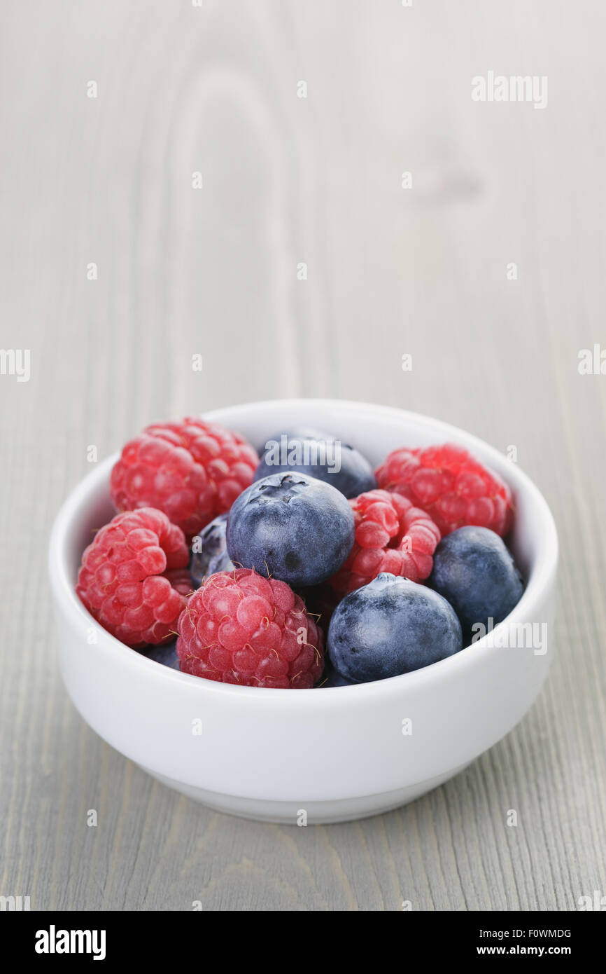 raspberries and blueberries in bowl on wood table Stock Photo - Alamy