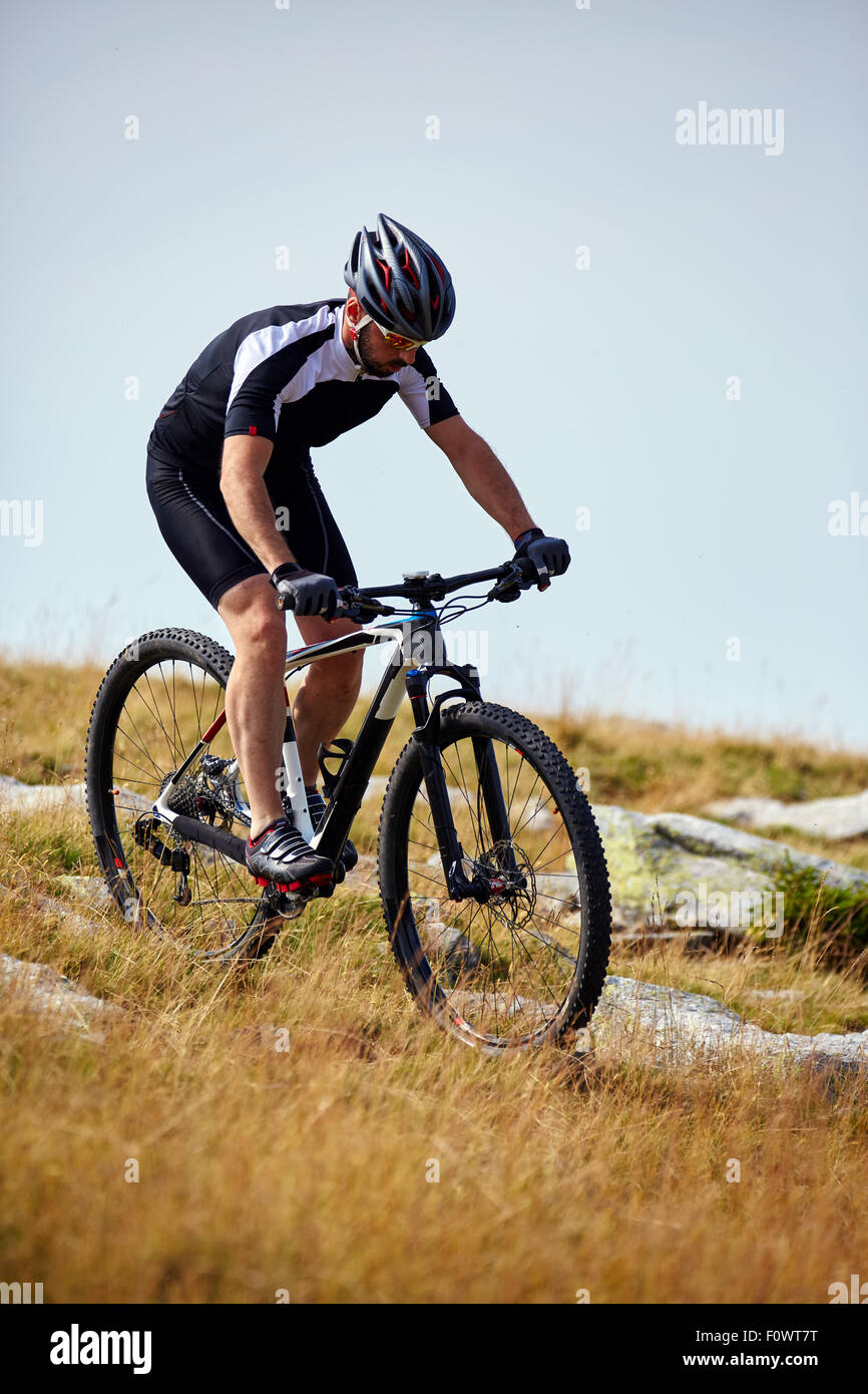 Mountain bike cyclist in sport equipment and helmet riding on rugged ...