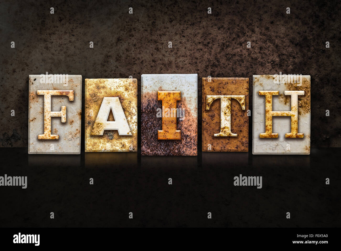 The word "FAITH" written in rusty metal letterpress type on a dark ...