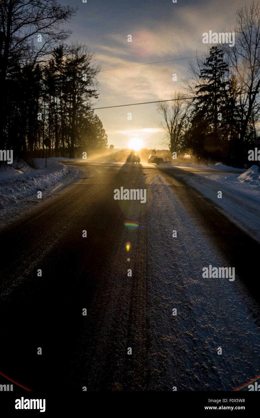 A snowy well-used road headed towards the sunset which is beginning to ...