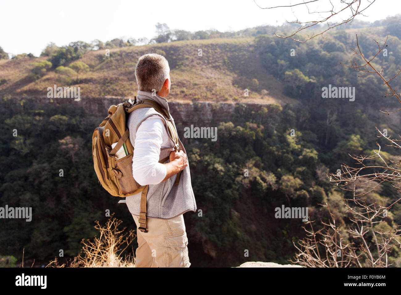 rear view of senior man with backpack standing on top of the mountain ...