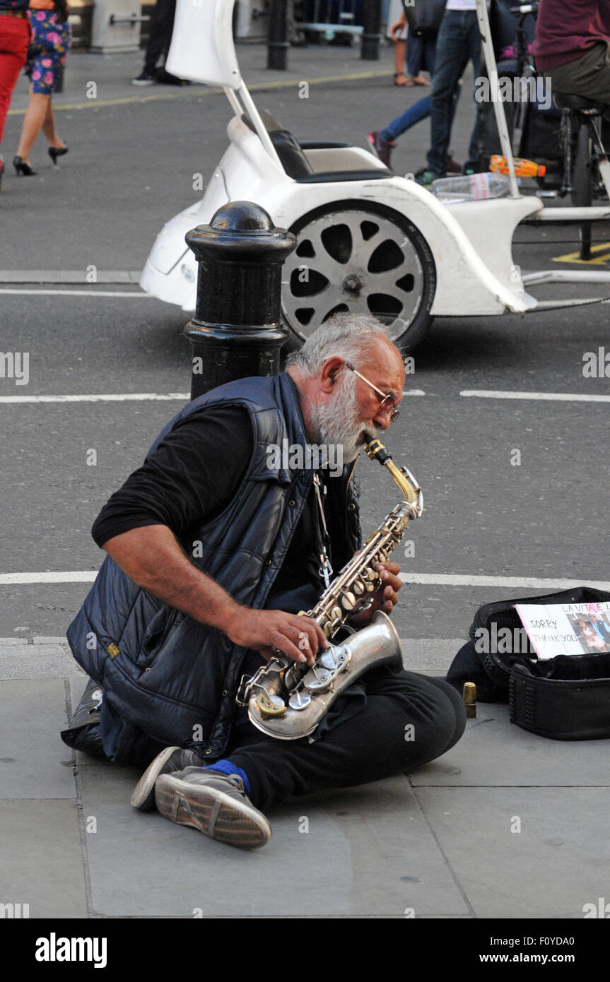 London, UK, 21/08/2015, Saxophone busker sits on the pavement playing ...